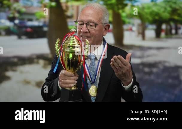 Senior man holding trophy outdoors wearing suit and medal while smiling ...