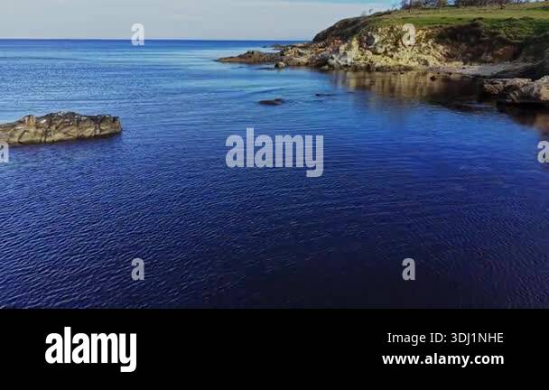 A tranquil coastal scene shows a deep blue sea meeting a rocky ...