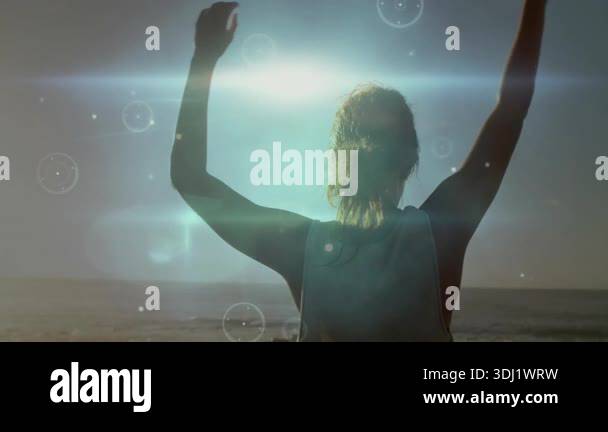 Woman raising arms on beach at sunset igniting pulsing light overlays ...