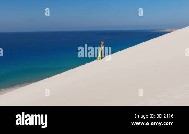 A woman in a green dress walks along the edge of a white sand dune ...