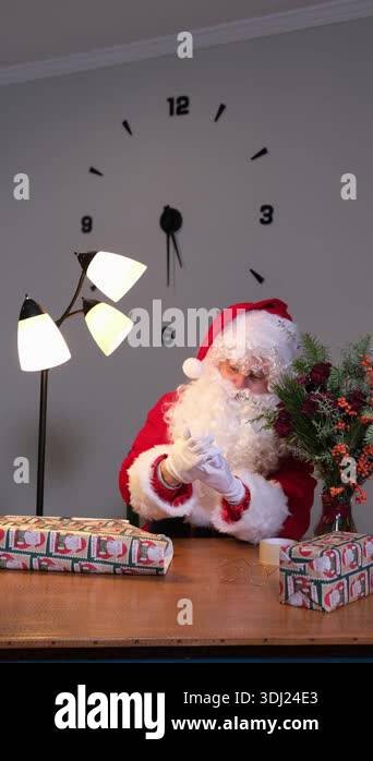 Traditional santa claus wrapping gifts at his desk under a large clock ...