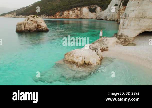 Woman exploring coastal rocks in hidden cove with emerald sea water and ...