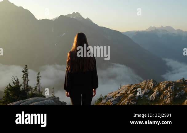 Young woman standing on a rocky slope, watching clouds drift over the ...