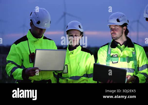 Engineers wearing safety helmets and jackets inspecting a wind turbine ...