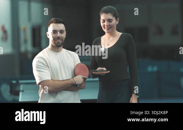 Young woman bounces a ping-pong ball on her paddle while a man stands ...