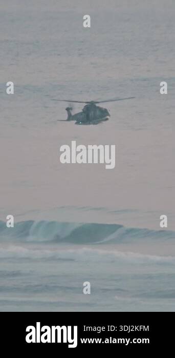 Military helicopter patrolling over a wavy ocean in overcast weather ...