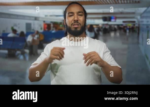 Man with beard and clasped hands at busy airport terminal in white t ...