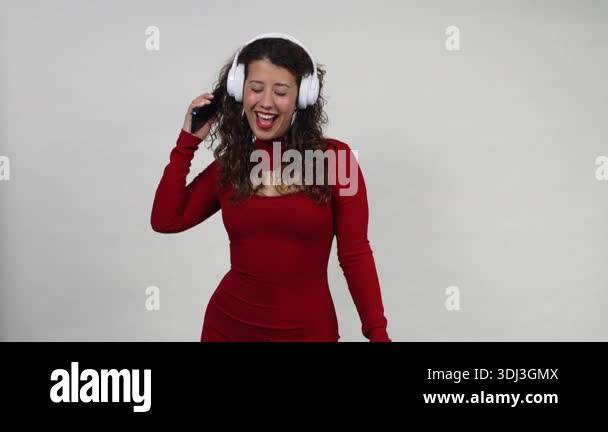 Cheerful curly woman wearing headphones listening to music and dancing ...
