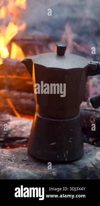 Moka pot brewing coffee over open campfire with burning wood, Outdoor ...