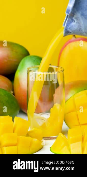 Freshly squeezed mango juice pouring from a jug into a glass, vertical ...