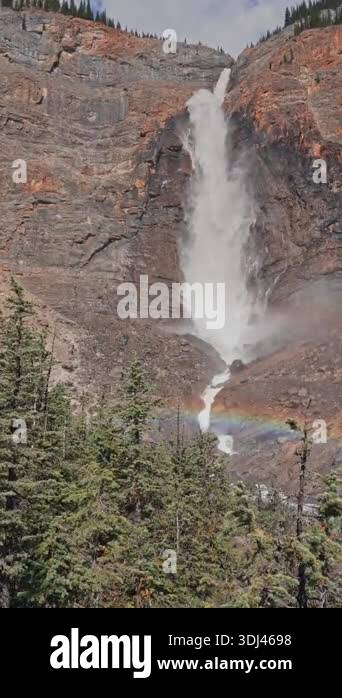 Waterfall cascading down rocky cliffside with rainbow. Takakkaw Fall ...