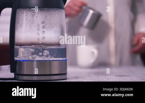 Boiling water in a kettle with woman making hot drink in background ...