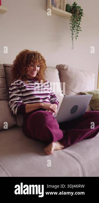 Young woman with curly red hair sitting comfortably on a couch, smiling ...