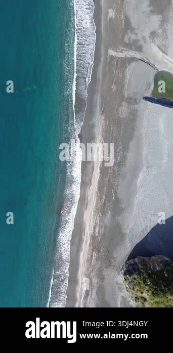 Vertical drone footage of a sandy coastline with winter waves crashing ...