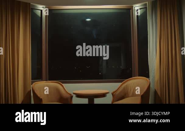 A laptop sits on a small round table between two armchairs in front of ...