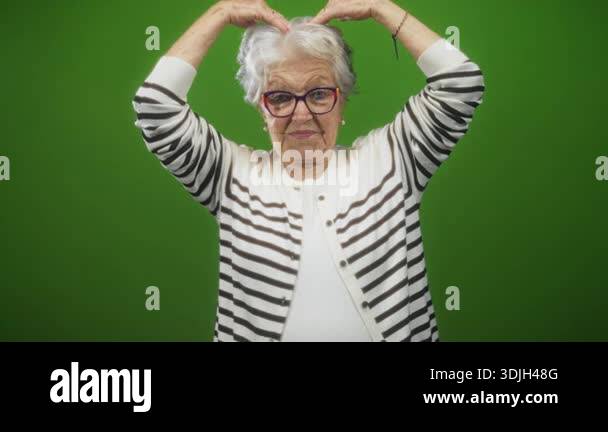 Senior woman forms hand heart over head while smiling, hands touching ...