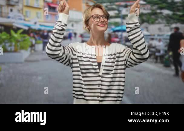 Woman pointing both index fingers and smiling, wearing glasses and ...