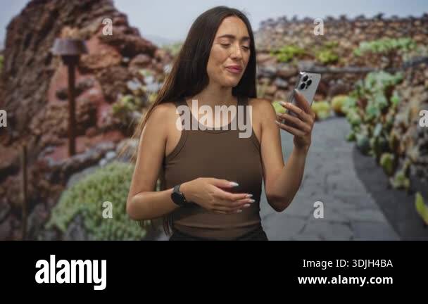 Woman holding smartphone and laughing with eyes closed in park pathway ...