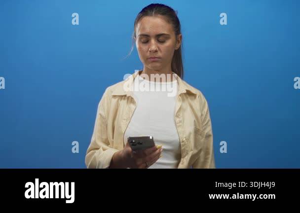Woman holding smartphone with fingers tapping the screen in blue studio ...