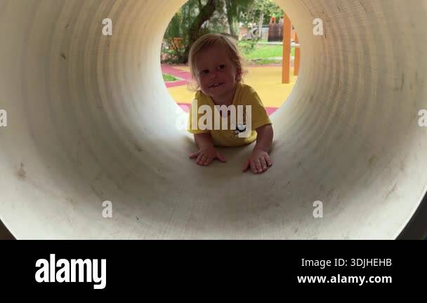 Toddler crawling inside a plastic tunnel at a childrens park, smiling ...