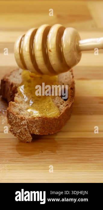 Golden honey drips from a wooden spoon onto a piece of rye bread ...