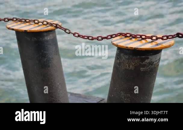 Two metal piles with a chain connect at a dock near the water Stock ...