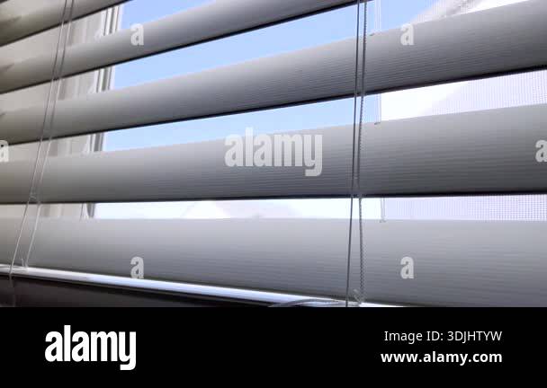 Horizontal metal blinds cover a window with daylight softly filtering ...