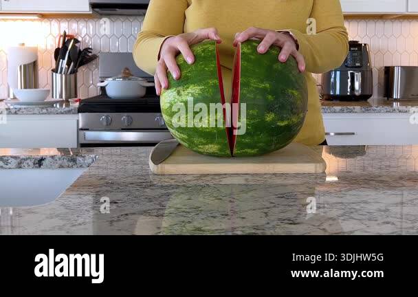 A woman in a yellow sweater slices a fresh watermelon on a cutting ...