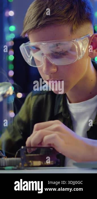 Likable smiling skillful teenage boy in protective glasses soldering ...