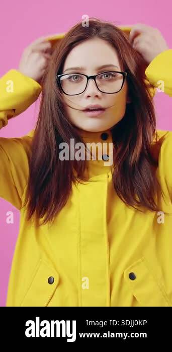 Woman in a yellow jacket stands against a pink background while posing ...