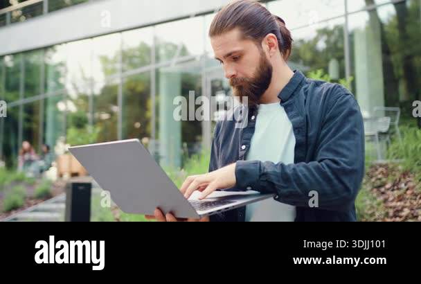 Handsome entrepreneur using a wireless laptop outdoors near a modern ...
