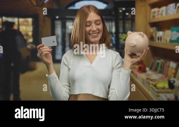 Young woman smiling in library holding piggy bank and credit card ...