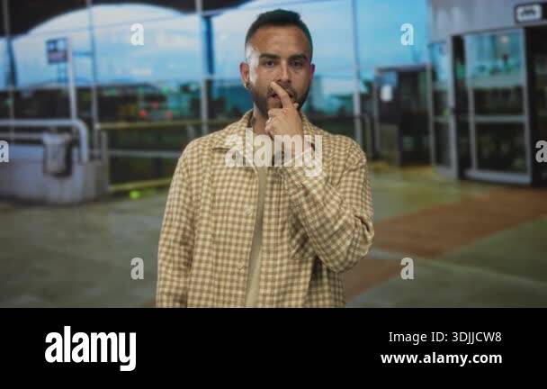 Man with finger to lips and visible hand on mouth at airport terminal ...