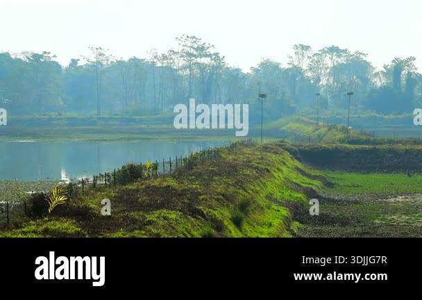 Wide view of a calm lake bordered by a green embankment and low fencing ...