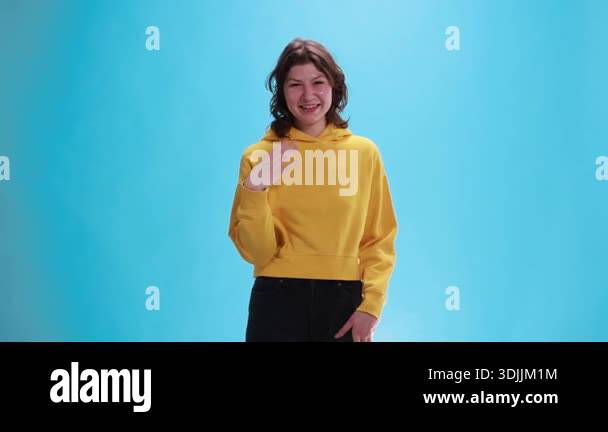 Young woman with playful smile touching hair on blue studio background ...