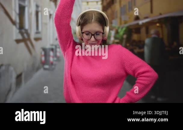 Young woman raises arm in pink sweater with white headphones on ...