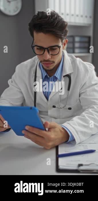 Young man in clinic wearing white coat using tablet, surrounded by ...