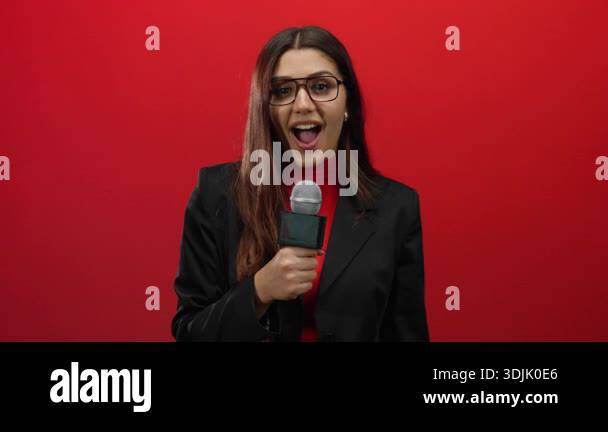 Young woman reporter holding microphone against vibrant red background ...