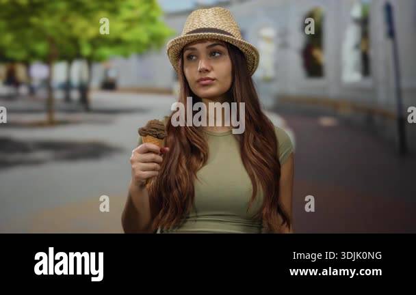 Woman eating ice cream outdoors wearing hat with brown long hair on ...