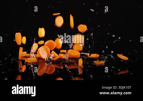 Sliced baby carrots fall and splash on a reflective black surface ...