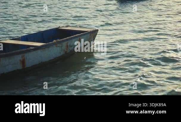 Rustic small wooden boat gently floating on rippling water, peaceful ...