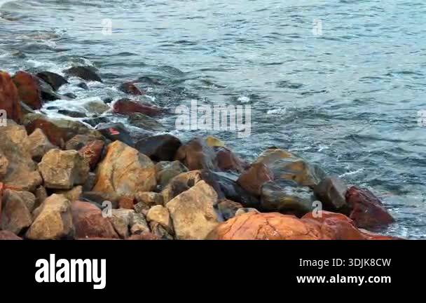 Water meets rocks at the shore during sunset near the coastline. Waves ...