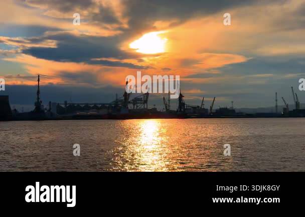 Sunset over a busy harbor with cranes and ships on the water. Sunset ...
