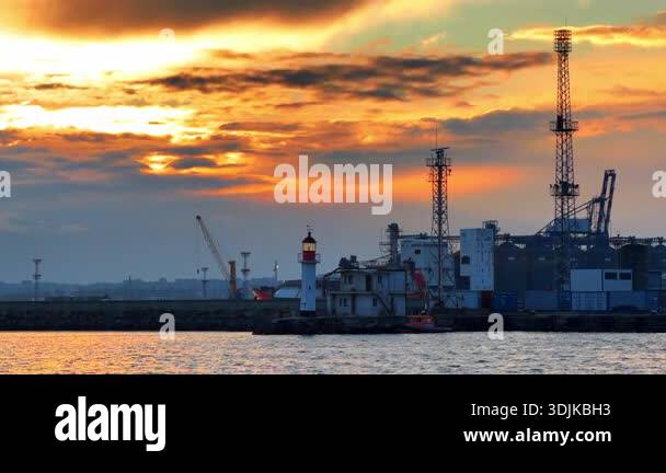Sunset over harbor with lighthouse and industrial structures in ...