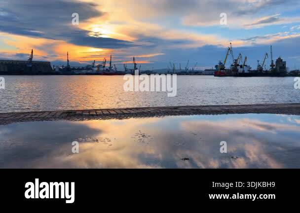 Sunset over a harbor with reflections in water and cranes in view ...