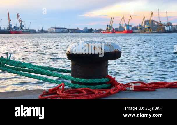 Rope tied around a mooring post near docks at sunset in a busy harbor ...