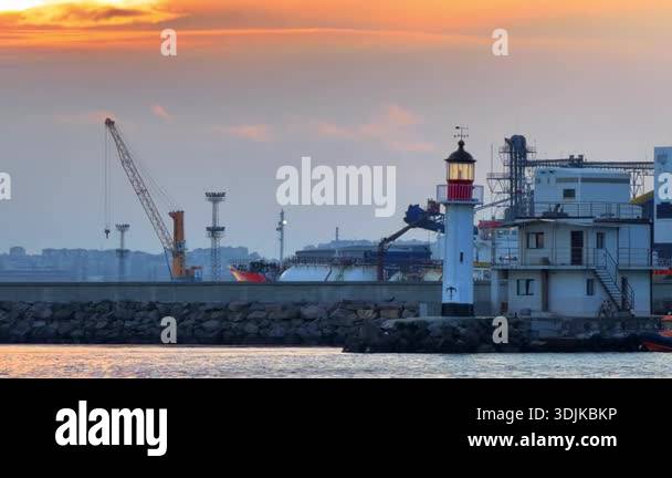Sunset view of harbor with lighthouse and buildings near water. The ...