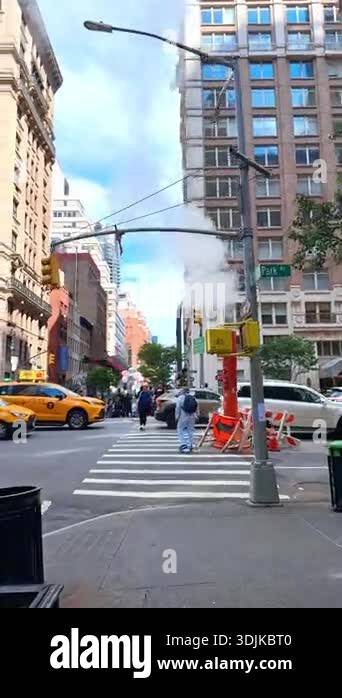 New York, USA, 24 May 2025: Crossroad produces white steam. Yellow taxi ...