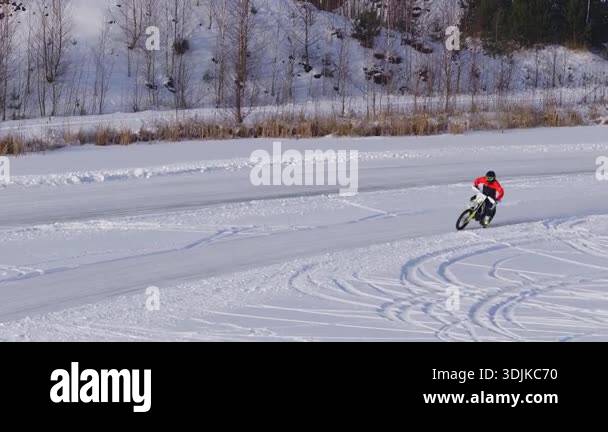 Aerial view shows a motorbike in a red jacket turning fast on a frozen ...