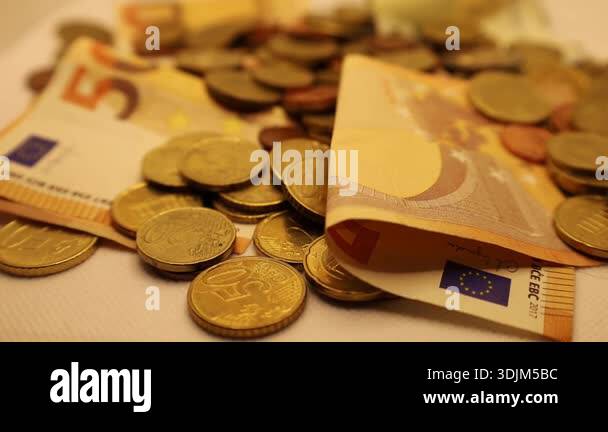 Many coins and euro notes are scattered on a flat surface with a focus ...